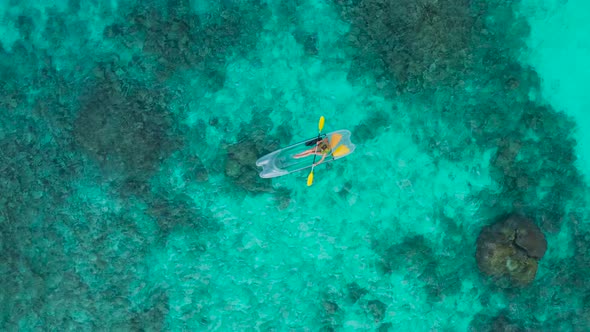 Aerial top view of young woman kayaking the floating transparent kayak ...