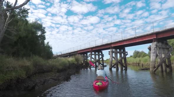 Tracking shot of a man in a red kayak paddling down a river with an old ...