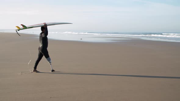 Long Shot of Man with Disability Going to Ocean with Surfboard, Stock ...