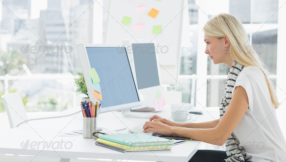 Side view of a casual young woman using computer in a bright office ...