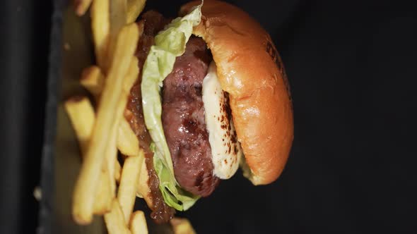 Fries falling on a burger in slow motion. Rotating vertical shot ...