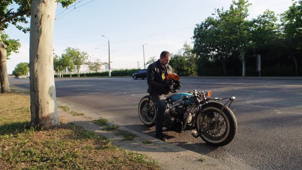 Young Man Biker with Custom Bobber Motorcycle on Street at Sunset ...