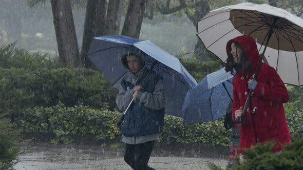 Kids in the pouring rain having fun jumping with umbrellas - slow ...