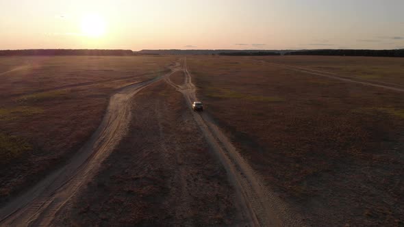 Aerial View of a Car Driving Off Into the Distance in a Meadow During a ...