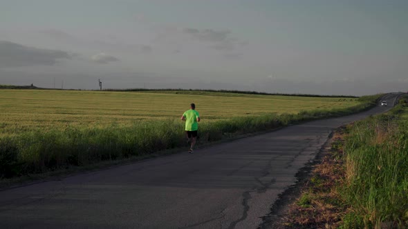 Man in neon green running past camera and wheat fields on spring ...