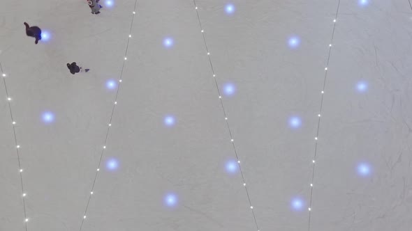 Aerial top-down ascending over lights and people skating on ice rink in ...