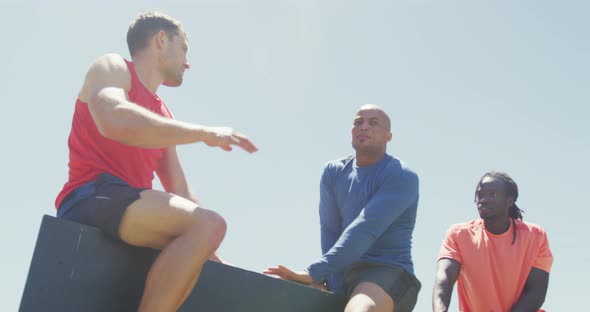 Three diverse fit men high fiving in the sun after climbing fence at ...