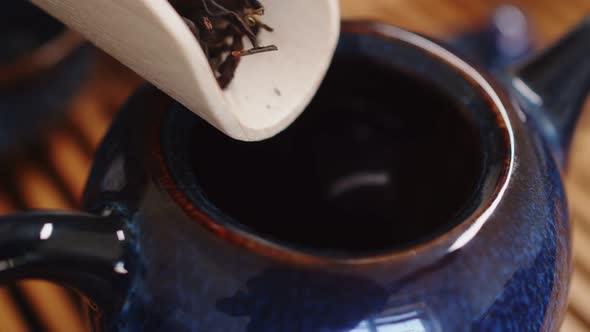Closeup of dry tea leaves spilling from a white wooden scoop into a ...