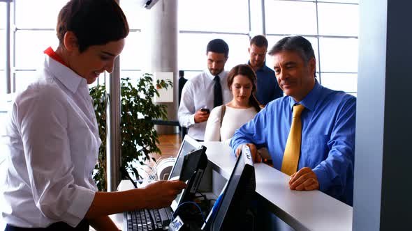Female airport staff checking passport of commuters at check-in desk ...