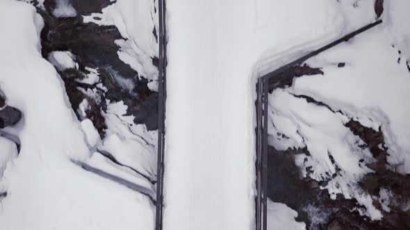 Aerial view of a small bridge over a creek in a snowy valley in the ...