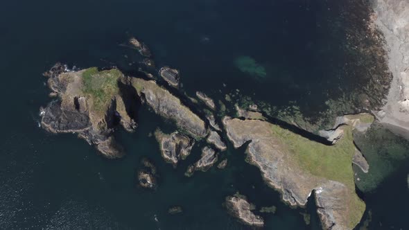 Ocean aerial ascends slowly from rugged steep rock islets near shore ...
