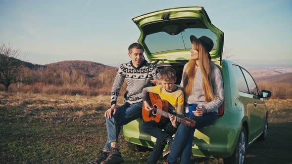 Family Plays Guitar and Sings Songs While Sitting on the Hatchback of ...