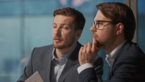 Two businessmen in suits listening to business partners at a meeting ...