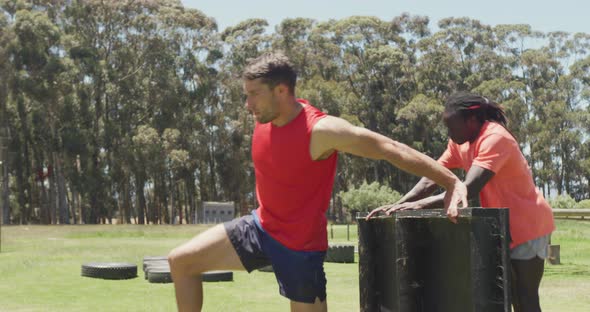 Two diverse fit men climbing over fences and running on obstacle course ...
