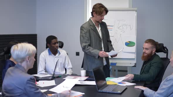 Serious Focused Male CEO Passing Paperwork to Employees Sitting at ...