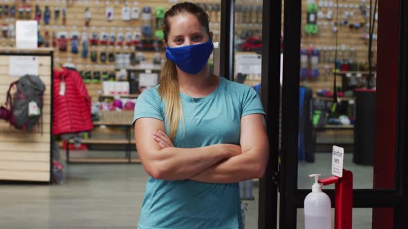 Caucasian female shopkeeper wearing face mask in the doorway of sports ...