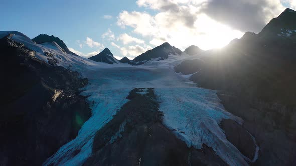 Aerial closeup sliding by snow-capped mountain peak against shining sun ...