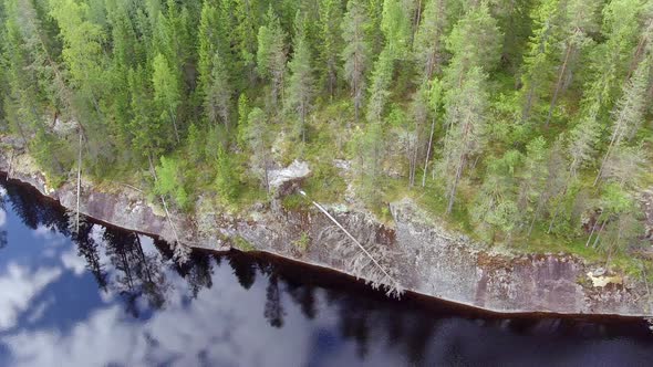 Aerial drone footage of the boreal wilderness. Old fallen pine trees on a steep cliff and mirror ...