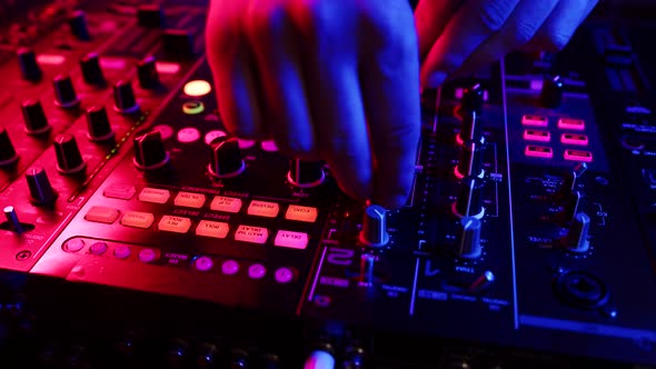 Closeup of hands of DJ tuning sound by turning knobs and pressing ...