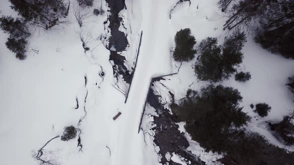 Aerial view of a small bridge over a creek in a snowy valley in the ...