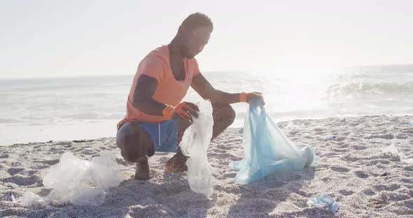African american man segregating waste with gloves on sunny beach ...