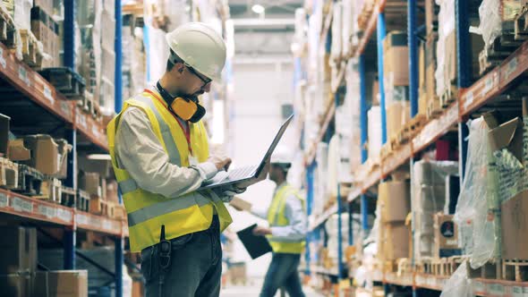 Storeman in Uniform Typing on Laptop Among Warehouse Shelves, Stock Footage