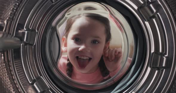 A Cute Happy Little Girl Looks Into the Washing Machine Through the ...