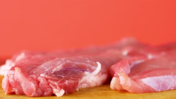 Close-up of pieces of raw red fatty pork meat rotate on a bright orange ...
