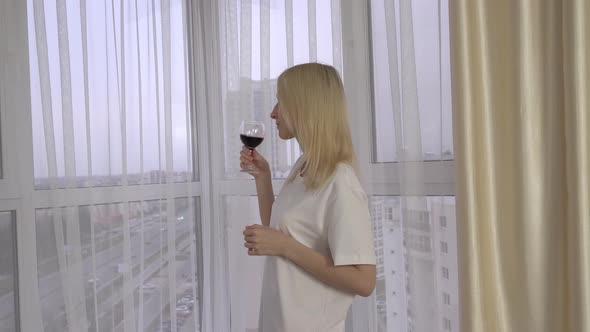 young, slender woman drinks wine, holds glass of red wine, and looks ...
