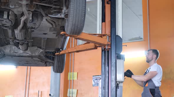 A Professional Car Mechanic Works Under the King of a Hoisting Machine ...