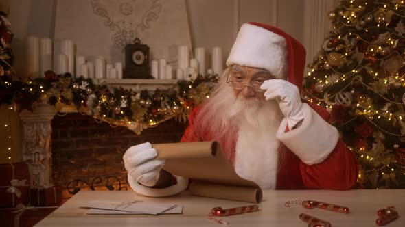 Santa Claus Reading Scroll Wishlist or Letter Sitting at His Desk Near ...