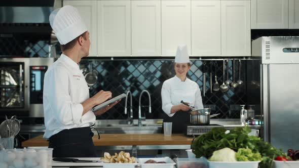 Restaurant kitchen: portrait of male and female cooks. Male Chef checks ...