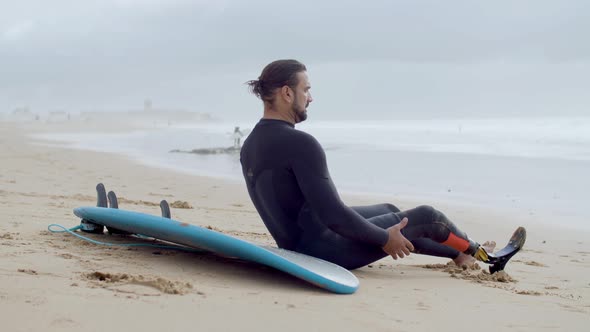 Tired Surfer with Bionic Leg Sitting on Ocean Shore, Stock Footage
