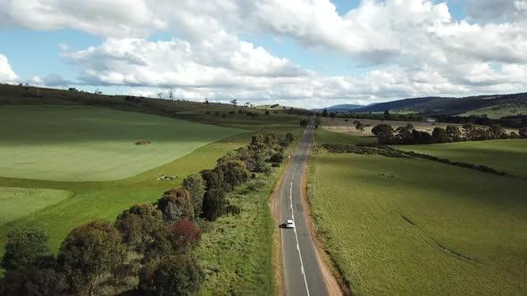 Drone Shot Of Car Driving Into Distance Along Country Road Lined By ...