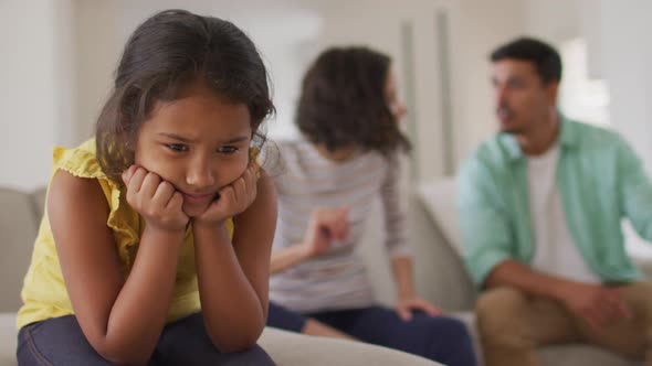 Sad hispanic girl sitting on sofa with parents arguing in background ...