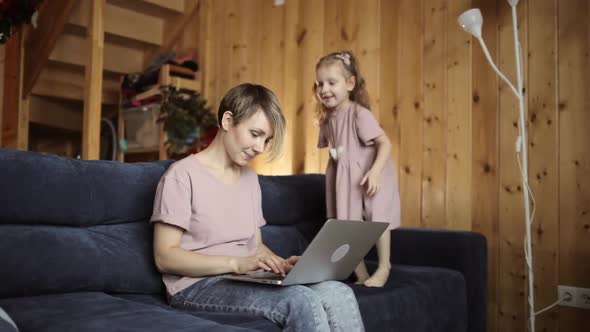 Mother Is Trying To Work on Laptop with Daughter Cuddling Her in Living ...