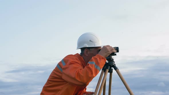 Skilled Surveyor in Orange Jumpsuit and Helmet at Theodolite, Stock Footage