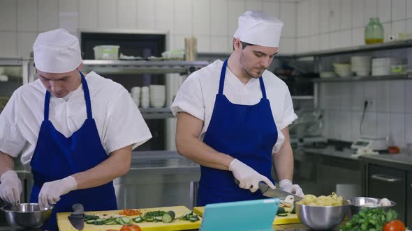 Front View Two Male Cooks Preparing Salad in Kitchen Talking, Stock Footage