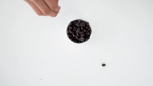 Top down view of throwing coffee bean into white bowl full of beans ...