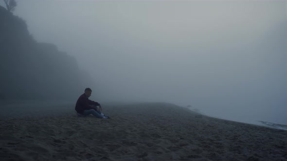 Depressed Guy Sitting Sea Beach in Foggy Morning, Stock Footage | VideoHive