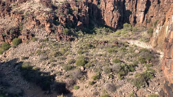 Upward tilt reveals rusty red shattered canyon walls in arid landscape ...