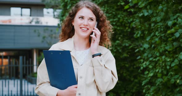 Young woman talks by phone, real estate agent or office worker outdoors ...