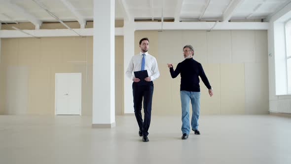 Businessman and manager walk around an empty warehouse discussing ...