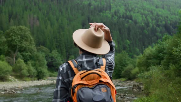 A Tourist Girl Puts On A Hat Standing Near The River, A Mountain River ...