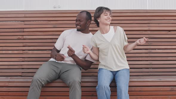 Multiethnic Couple Dancing while Sitting on Bench Outdoors, Stock Footage