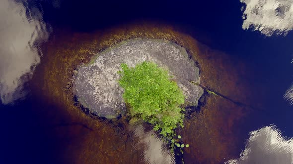 Ascending drone video of a very small rock island at the center of a ...
