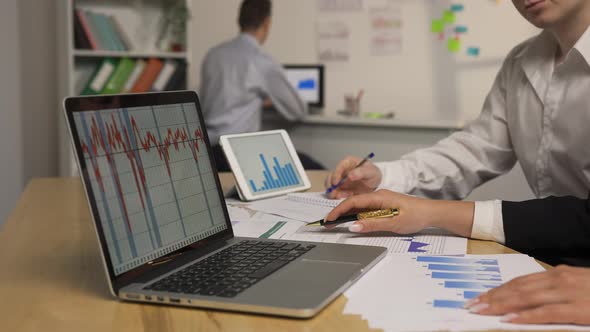 Man and Woman Viewing Papers with Charts and Graphs Using Laptop Tablet ...