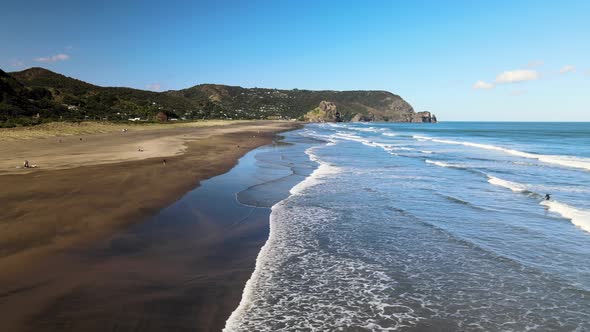 Panning across Piha black sand beach with reflection of surfer walking ...
