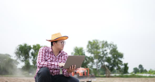 Man squatting in corn field using laptop with tractor, Stock Footage