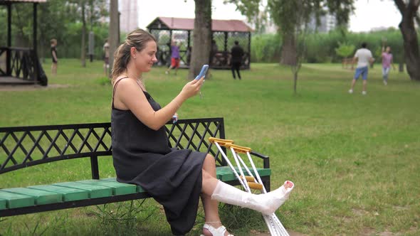 A Young Girl with a Cast and Crutches is Sitting in the Park Watching ...